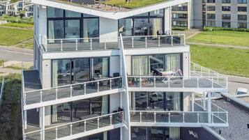 Um edifício moderno de vários andares com varandas de vidro e áreas de estar ao ar livre.