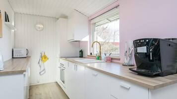 Cozinha moderna com armários brancos, bancada de madeira, máquina de café e janela com vista para árvores.