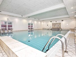 Uma piscina interior ampla com chão em mosaico e superfície de água transparente.