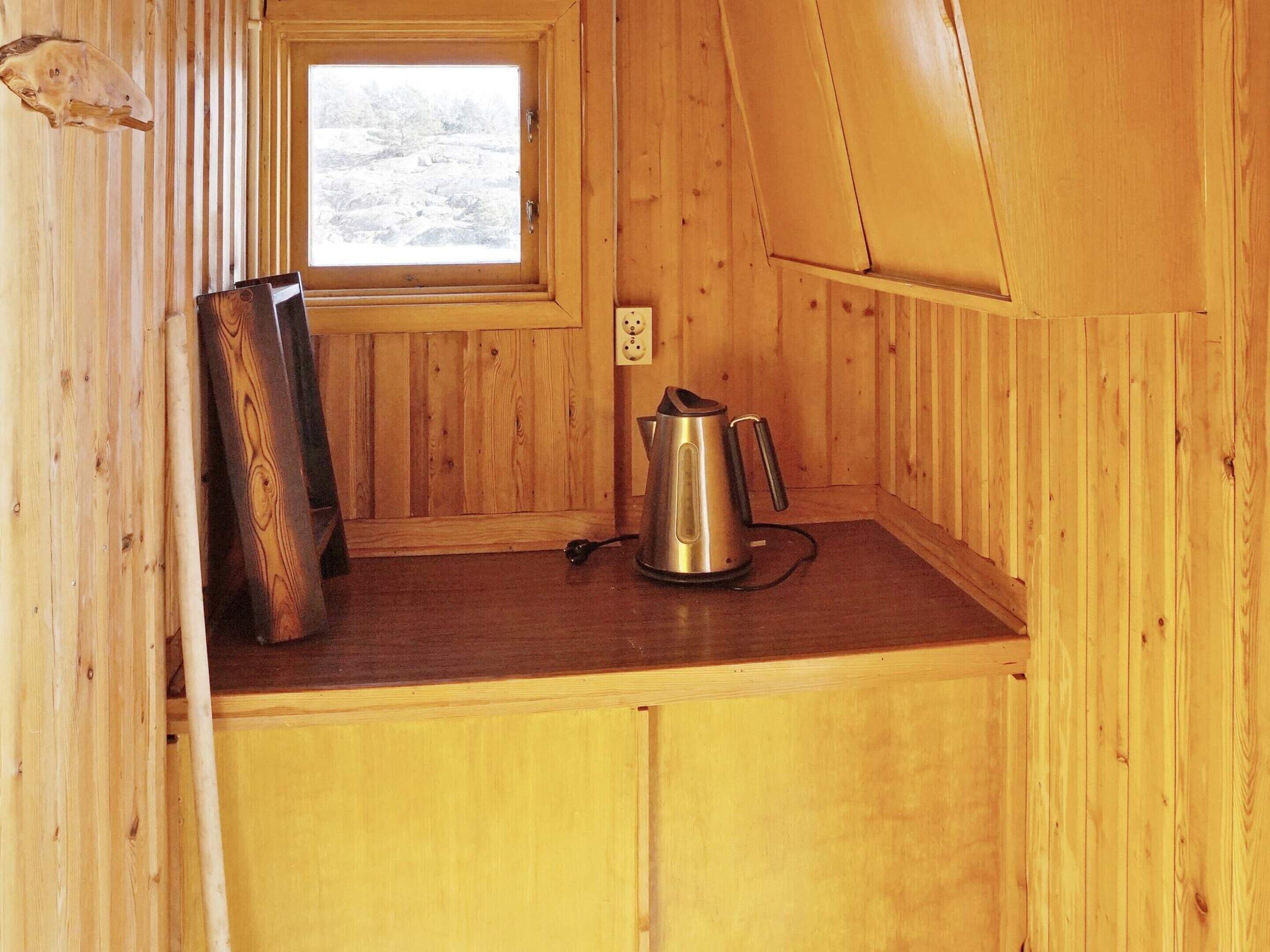 Interior de cabana de madeira com janela, chaleira e porta de madeira.