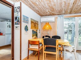 Uma sala de jantar com mesa e cadeiras de madeira, uma luminária pendente e vista para o exterior através de uma porta de vidro.