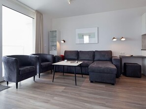 Uma sala de estar moderna com um conjunto de sofás, uma mesa de centro e uma escrivaninha com duas luminárias.