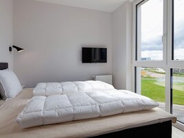 Quarto com cama grande, televisão montada e vista para uma paisagem verde pela janela.