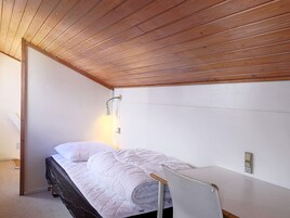 Quarto com uma cama, mesa de cabeceira, abajur e teto de madeira.