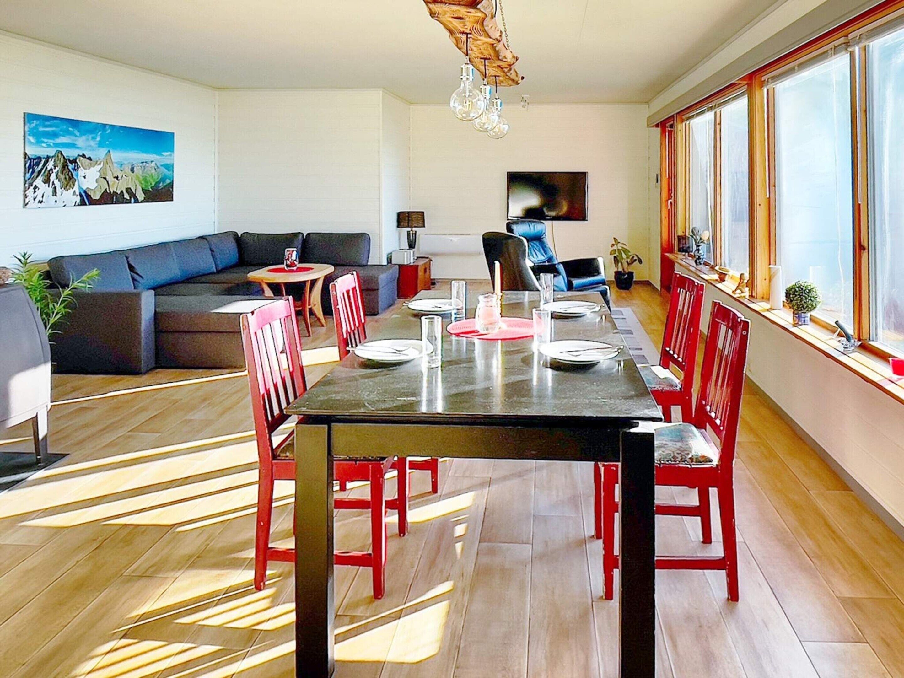 Uma sala de jantar com uma mesa comprida, cadeiras vermelhas e um lustre moderno.