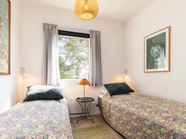 Quarto com duas camas de solteiro, janela com cortinas, luminária de pé e quadro na parede.