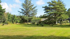 Um campo gramado com árvores e uma casa ao fundo.