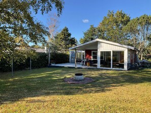 Uma casa moderna com alpendre coberto, espaço para churrasco e gramado.