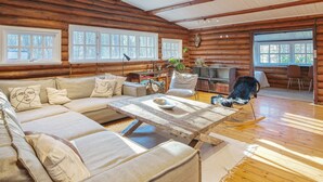 Interior de uma cabana de madeira com sofás, uma mesa de centro e uma estante de livros.
