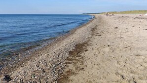 Uma praia de seixos com águas cristalinas e uma vista distante de colinas.