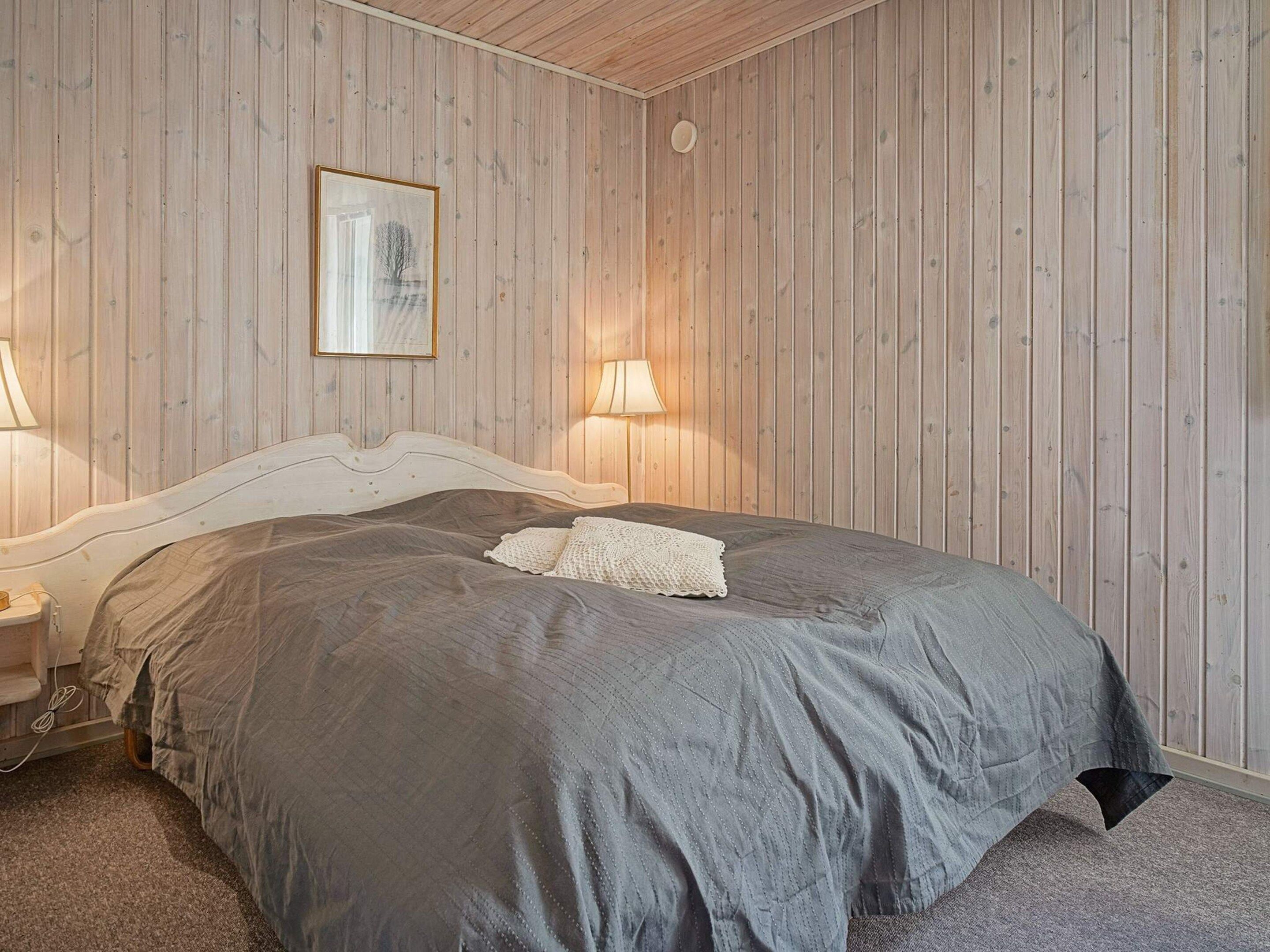 Quarto com cama, mesa de cabeceira, luminária e quadro na parede.