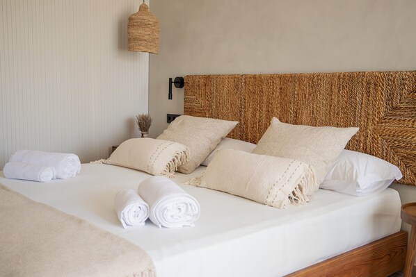 Cama bem arrumada com toalhas brancas dobradas, cabeceira de tecido e abajur.