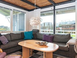 Uma sala de estar moderna com um sofá seccional, uma mesa de centro de madeira e grandes janelas com vista para o exterior.