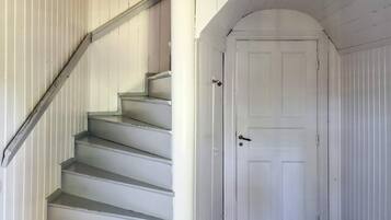 Escada de madeira branca que leva a uma porta branca com corrimão de metal.