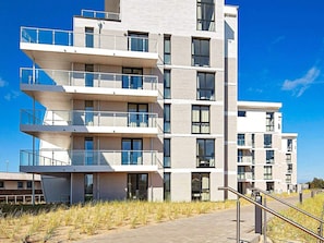 Um edifício residencial com vários andares, varandas, janelas amplas e céu claro.