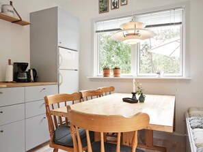 Cozinha compacta com mesa e cadeiras, cafeteira e geladeira.