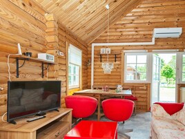 Interior de cabana com decoração em madeira, televisão, mesa de jantar com cadeiras e uma janela.