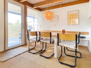 Uma área de refeições com mesa de madeira e quatro cadeiras de estrutura preta, luminária pendente laranja e obra de arte Bauhaus emoldurada na parede.