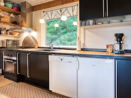 Cozinha moderna com máquina de lavar louça, forno e janela com vista para o verde.