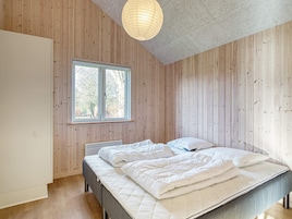 Quarto com cama, janela e paredes de madeira.