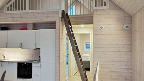 Cozinha moderna com armários brancos, forno embutido e escada de madeira que dá acesso a um quarto no mezanino.