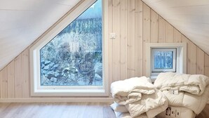 Um quarto com teto inclinado, uma janela grande com vista para uma paisagem rochosa e uma cama com edredom branco.