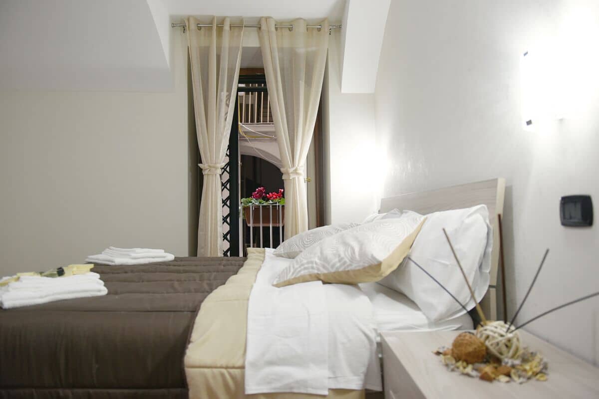 Quarto de hotel com cama, mesa de cabeceira e janela com cortinas.