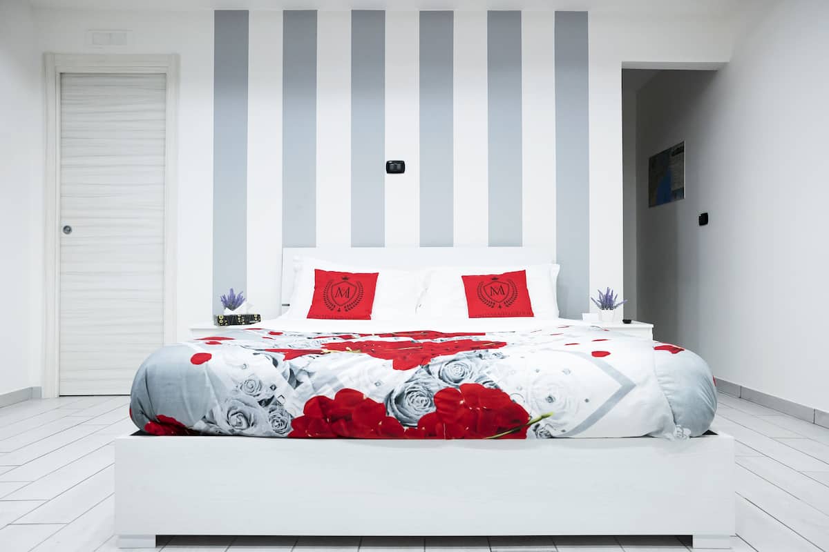 Quarto moderno com cama branca, parede listrada em vermelho e cinza, e porta branca.