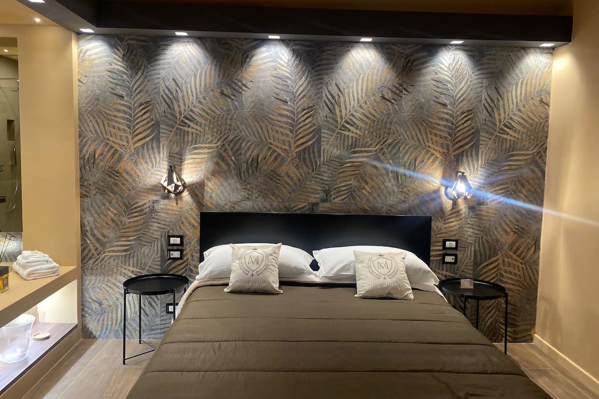 Quarto moderno com uma cama grande, duas mesas de cabeceira e uma parede com padrão de folhas.