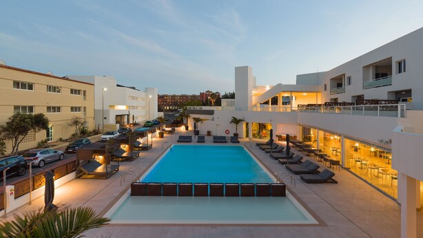 Uma área de piscina no terraço com espreguiçadeiras, piscina e vista para edifícios ao redor.
