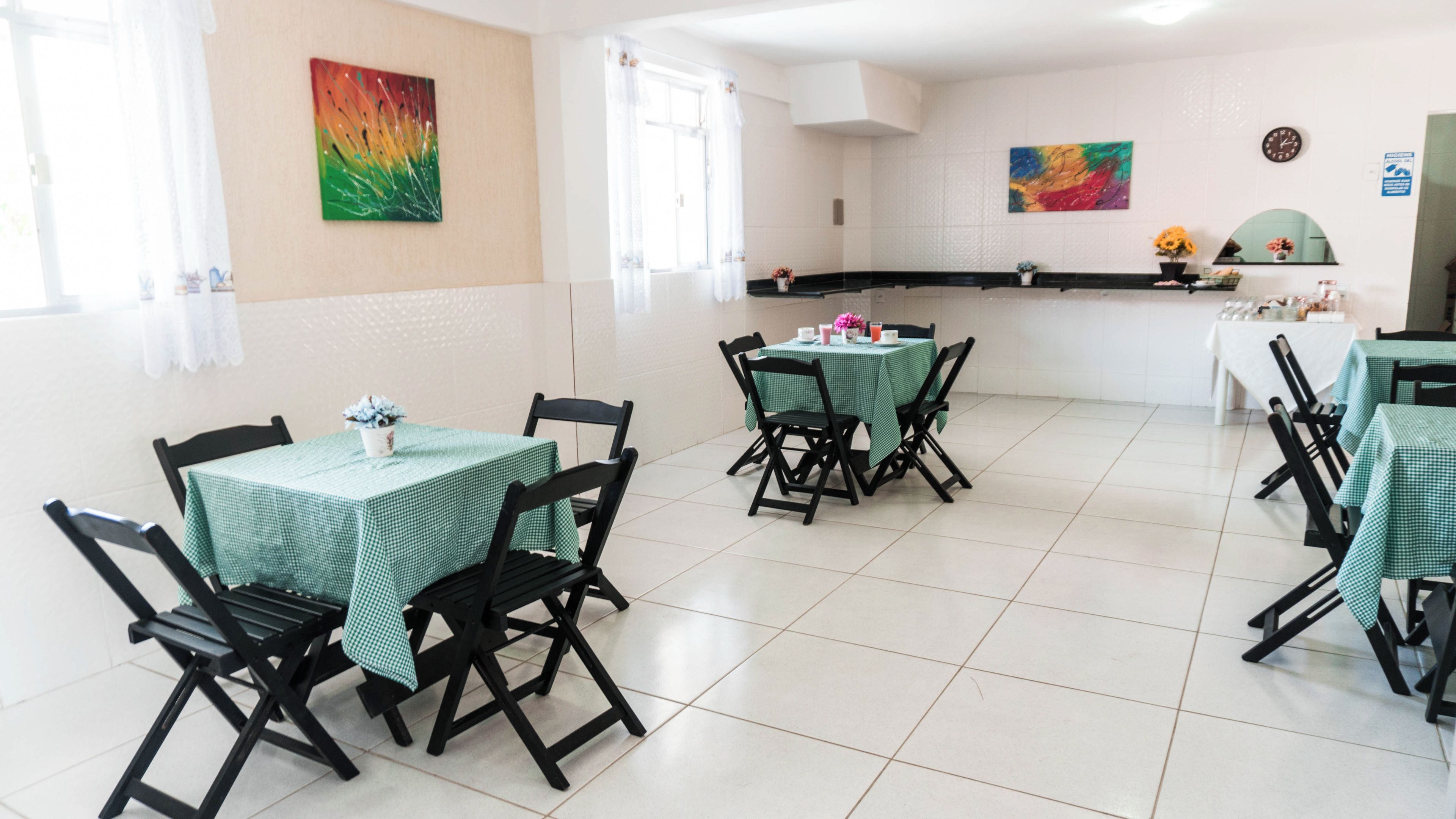 Uma sala de jantar com mesas e cadeiras, bancada de cozinha e obras de arte nas paredes.