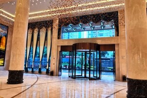 Um saguão com colunas de mármore, uma porta giratória e vista para o exterior.