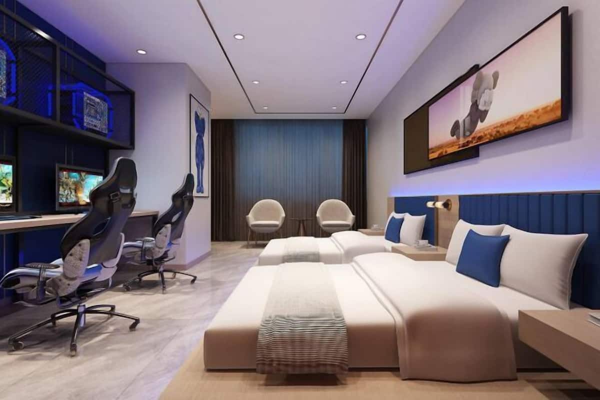 Quarto de hotel moderno com uma cama grande, uma mesa com cadeiras de jogos, uma televisão e um quadro grande na parede.