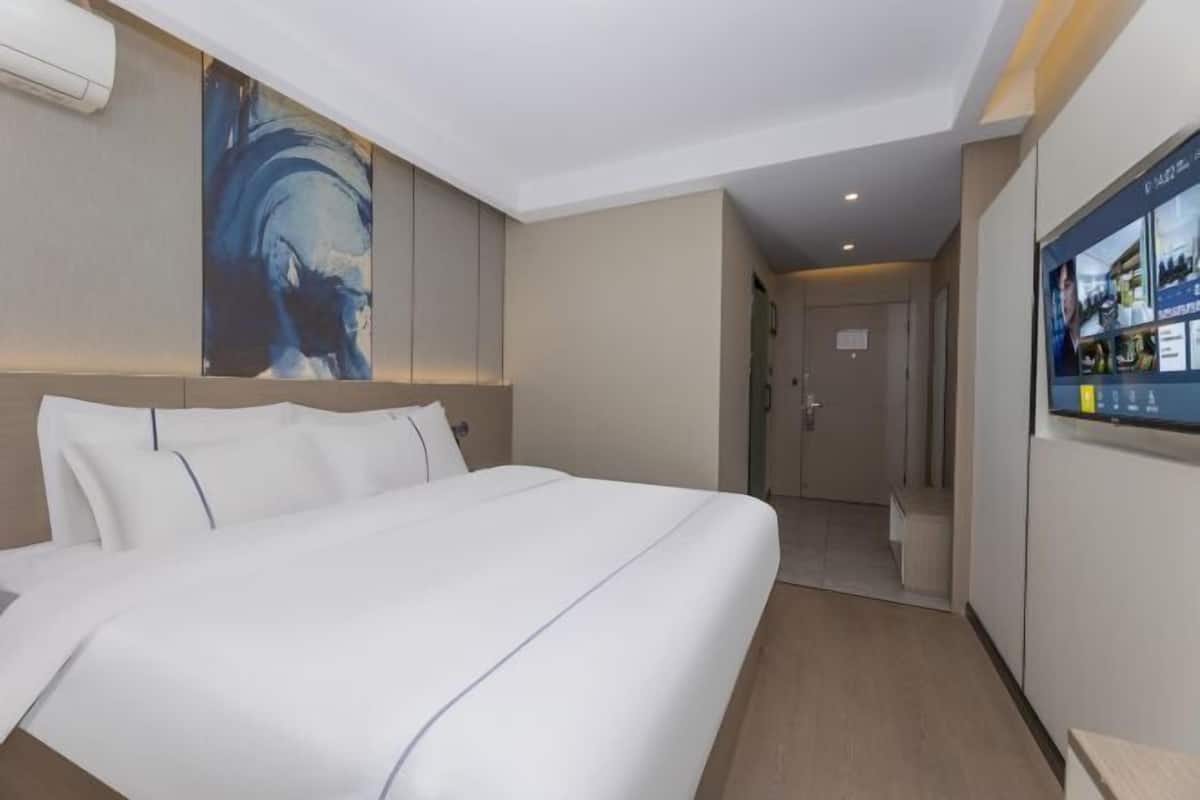 Quarto de hotel com uma cama grande, uma televisão de tela plana na parede e um quadro sobre a cama.