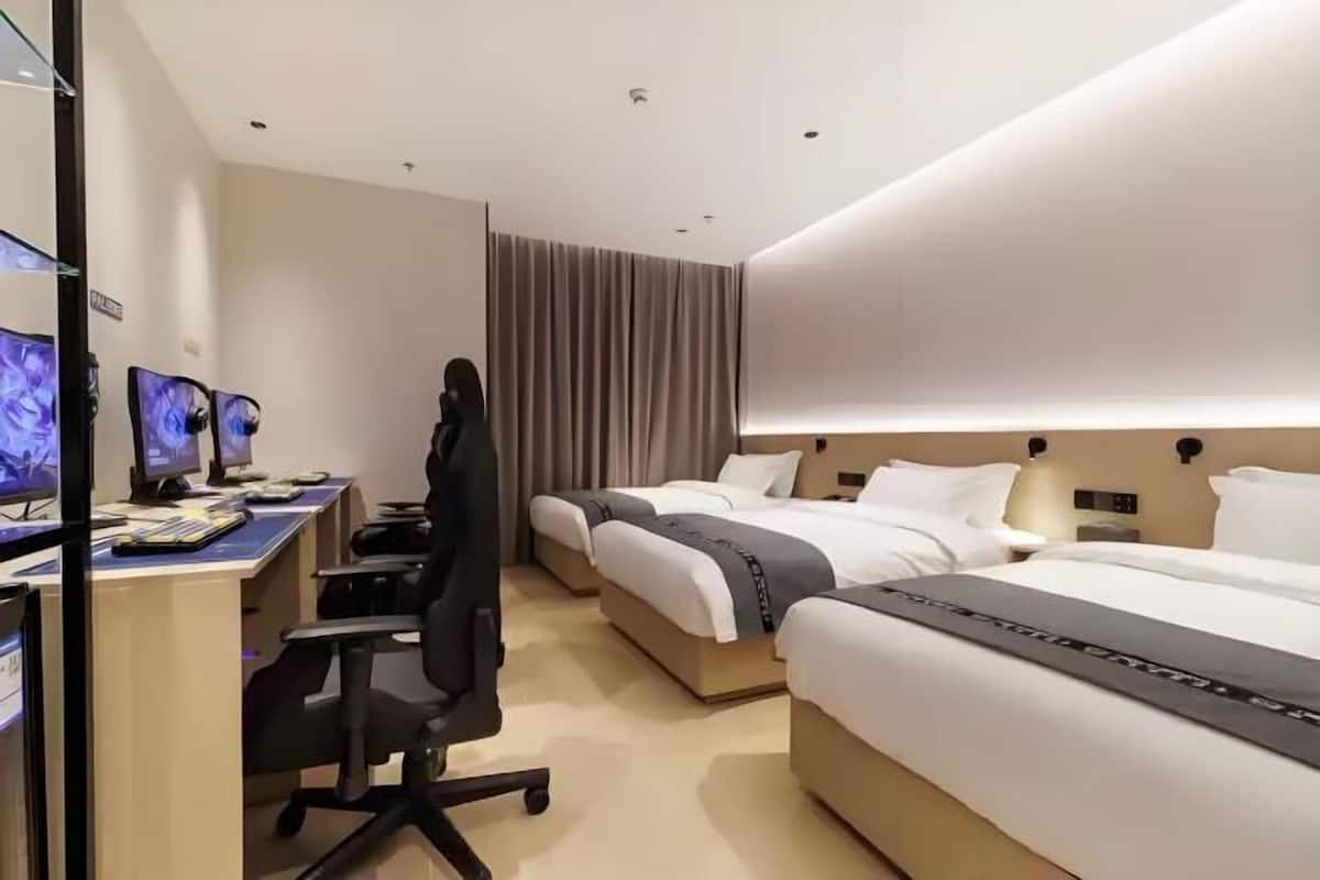 Quarto de hotel com duas camas, uma escrivaninha com computador e uma cadeira.