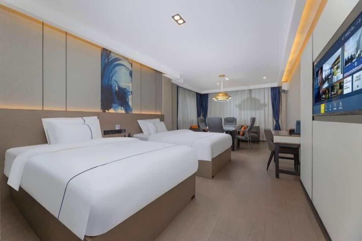 Quarto de hotel com duas camas, uma escrivaninha, uma cadeira, uma televisão e um quadro abstrato grande na parede.
