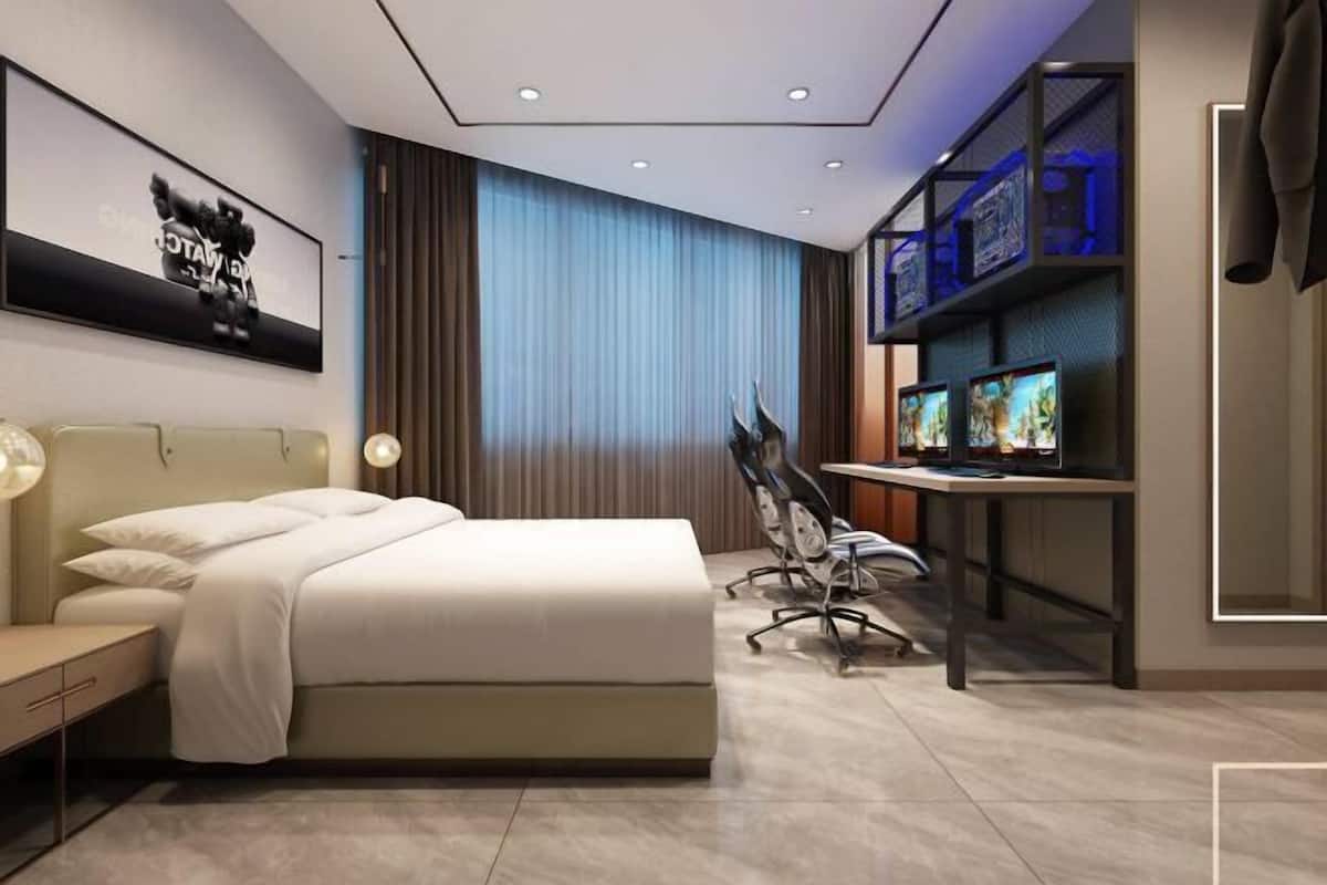 Quarto de hotel moderno com uma cama, escrivaninha e dois monitores.