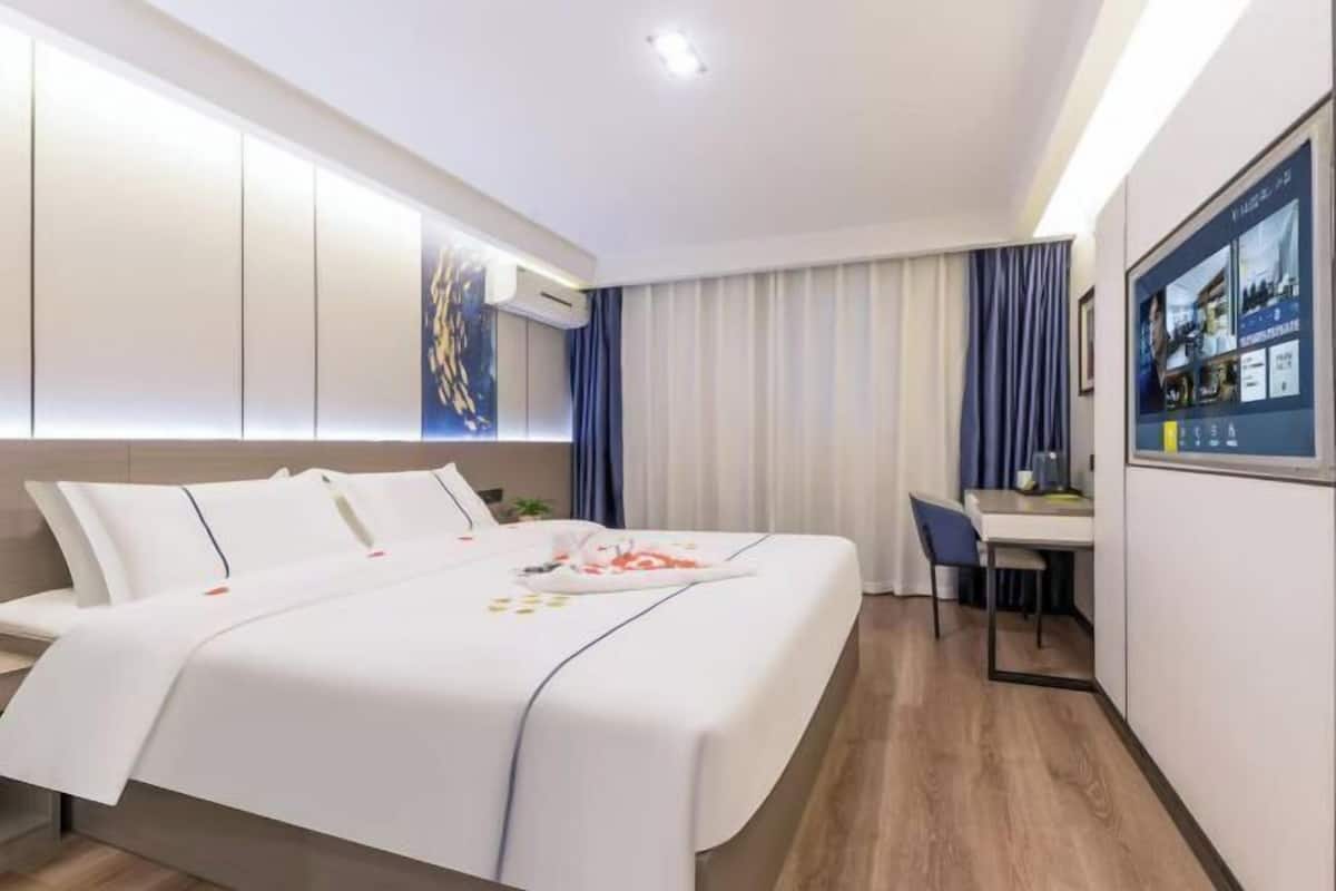 Quarto de hotel moderno com uma cama grande, uma escrivaninha e uma televisão na parede.