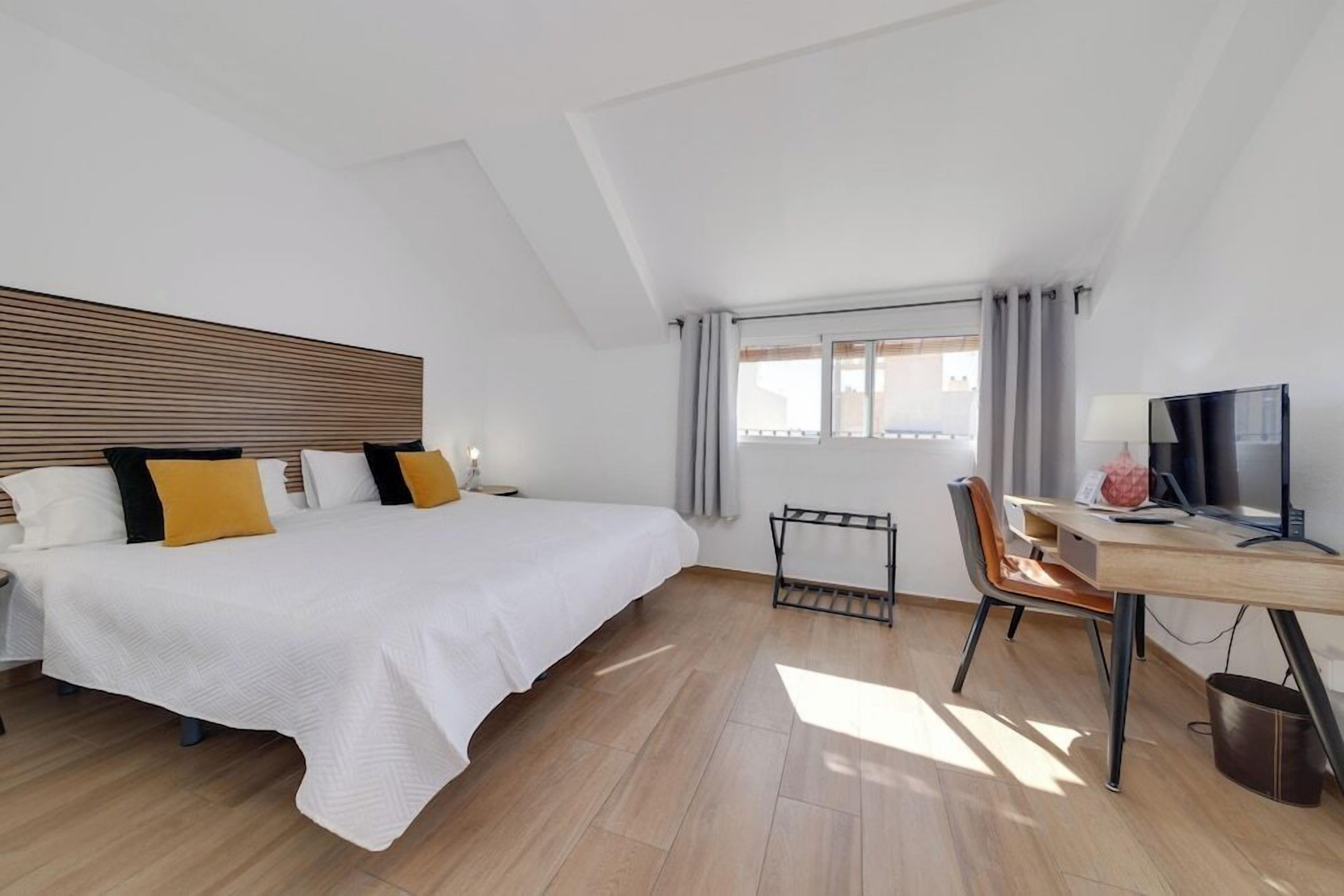 Quarto de hotel moderno com uma cama grande, uma escrivaninha com computador e uma televisão.