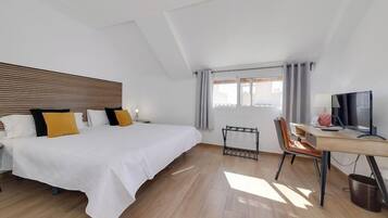 Quarto de hotel moderno com uma cama grande, uma escrivaninha com computador e uma televisão.