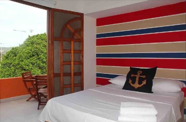 Quarto com cama, uma cadeira de madeira e vista para o verde lá fora.