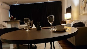Uma sala de jantar com uma mesa redonda e cadeiras, um pequeno vaso e duas taças de vinho.