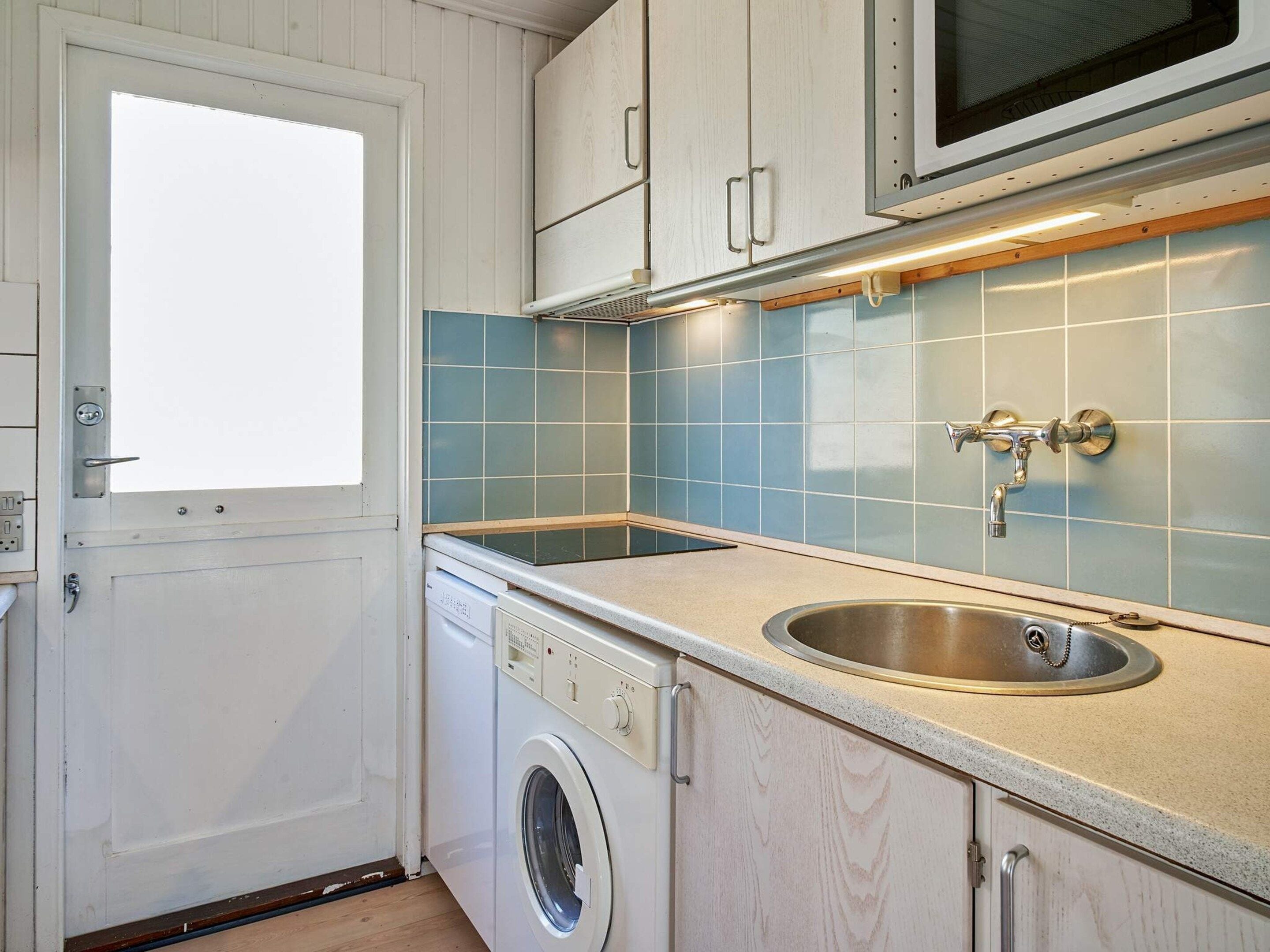 Cozinha compacta com máquina de lavar embutida, pia e micro-ondas sobre a bancada.