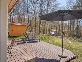 Um deck de madeira com móveis de exterior e um galpão numa área arborizada.