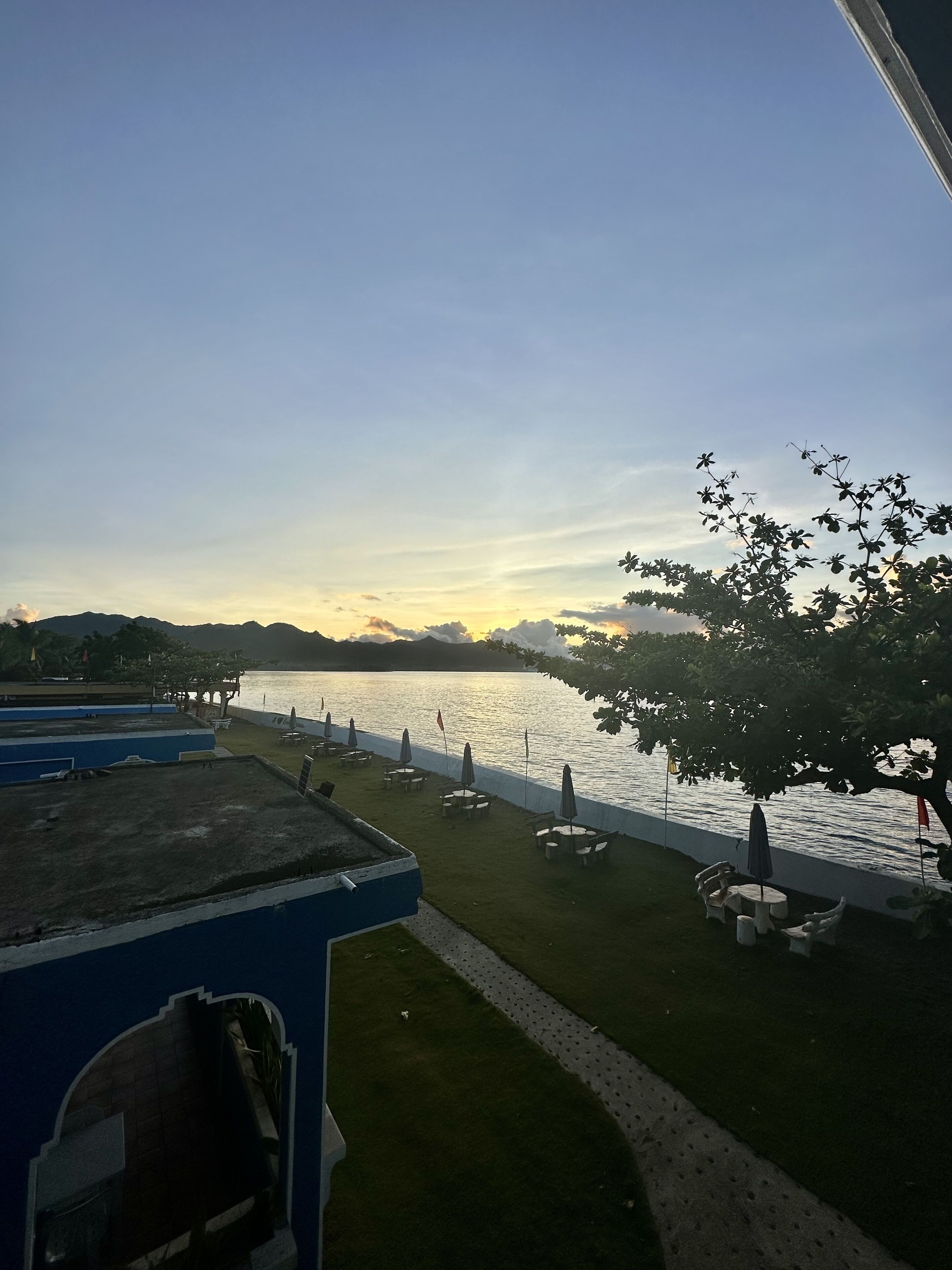 Um terraço à beira do lago com mesas e cadeiras, um caminho e vista para a água.