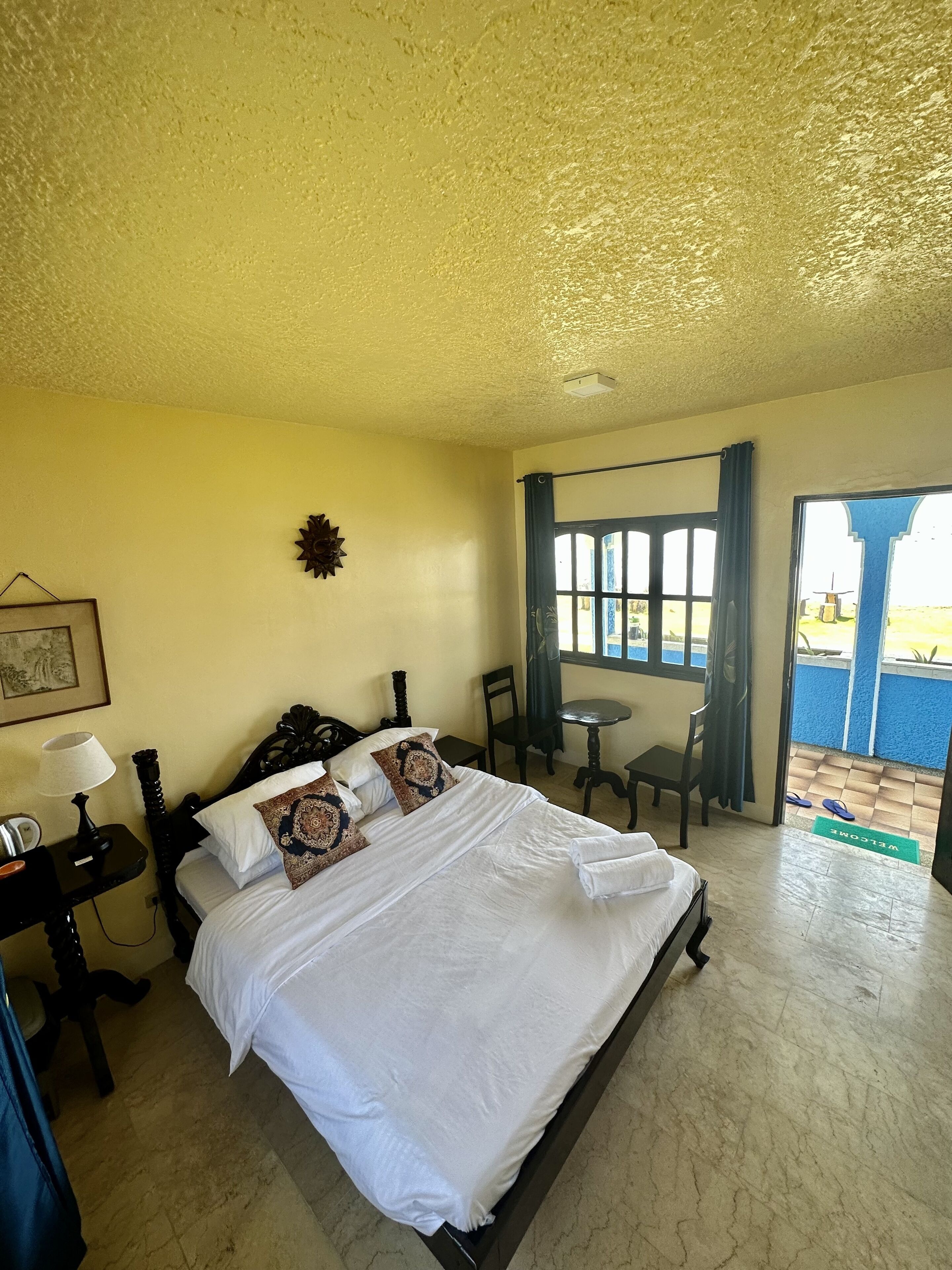 Quarto de hotel com cama, escrivaninha, cadeira e janela com cortinas.
