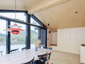 Uma sala de jantar moderna com mesa de madeira, cadeiras pretas e luminária pendente vermelha.