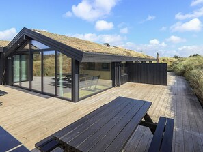 Um edifício moderno com fachada de vidro, deck de madeira e área de estar ao ar livre.