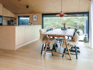 Cozinha moderna com armários de madeira, mesa de jantar com cadeiras e uma janela grande com vista para o verde.