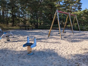 Um parquinho arenoso com balanço e gangorra.